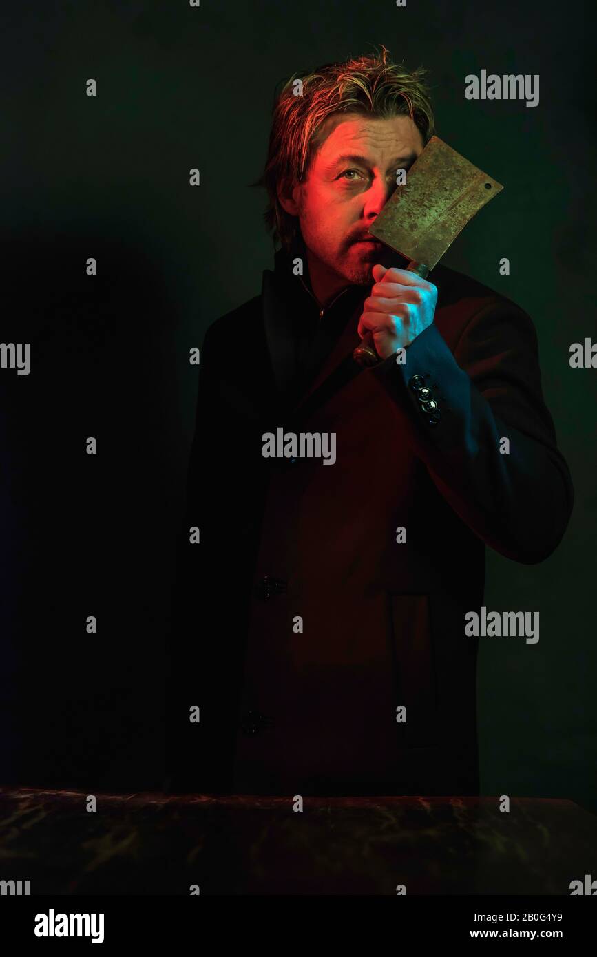 Man holding meat cleaver in front of face. Standing in red and green ...