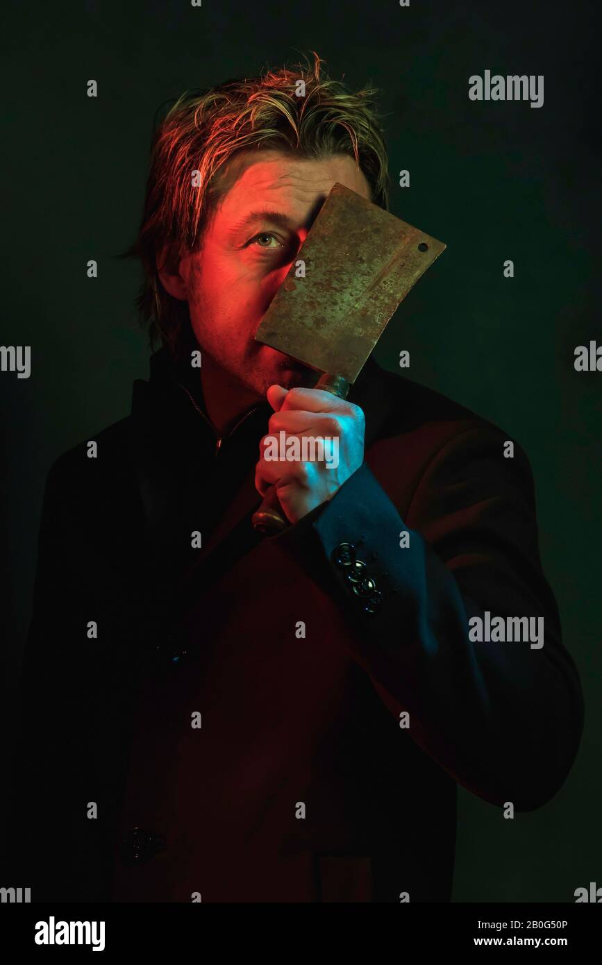 Man holding meat cleaver in front of face. Standing in red and green ...