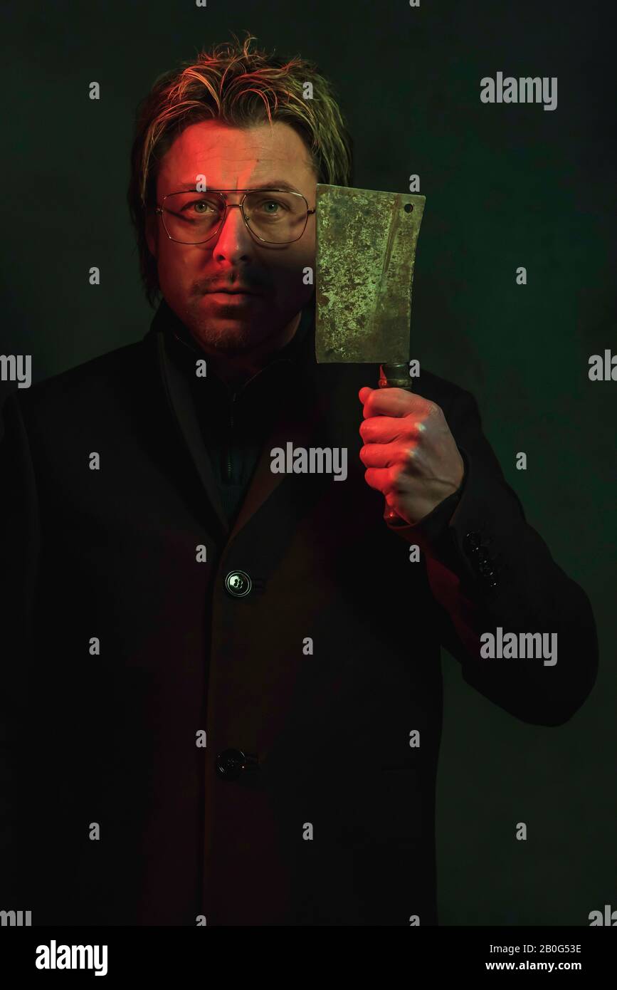 Man holding meat cleaver near his face. Illuminated by red and green ...