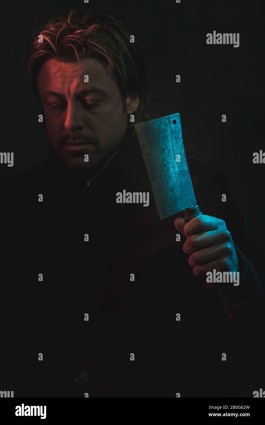 Threatening man with cleaver in hand illuminated by red and blue light ...