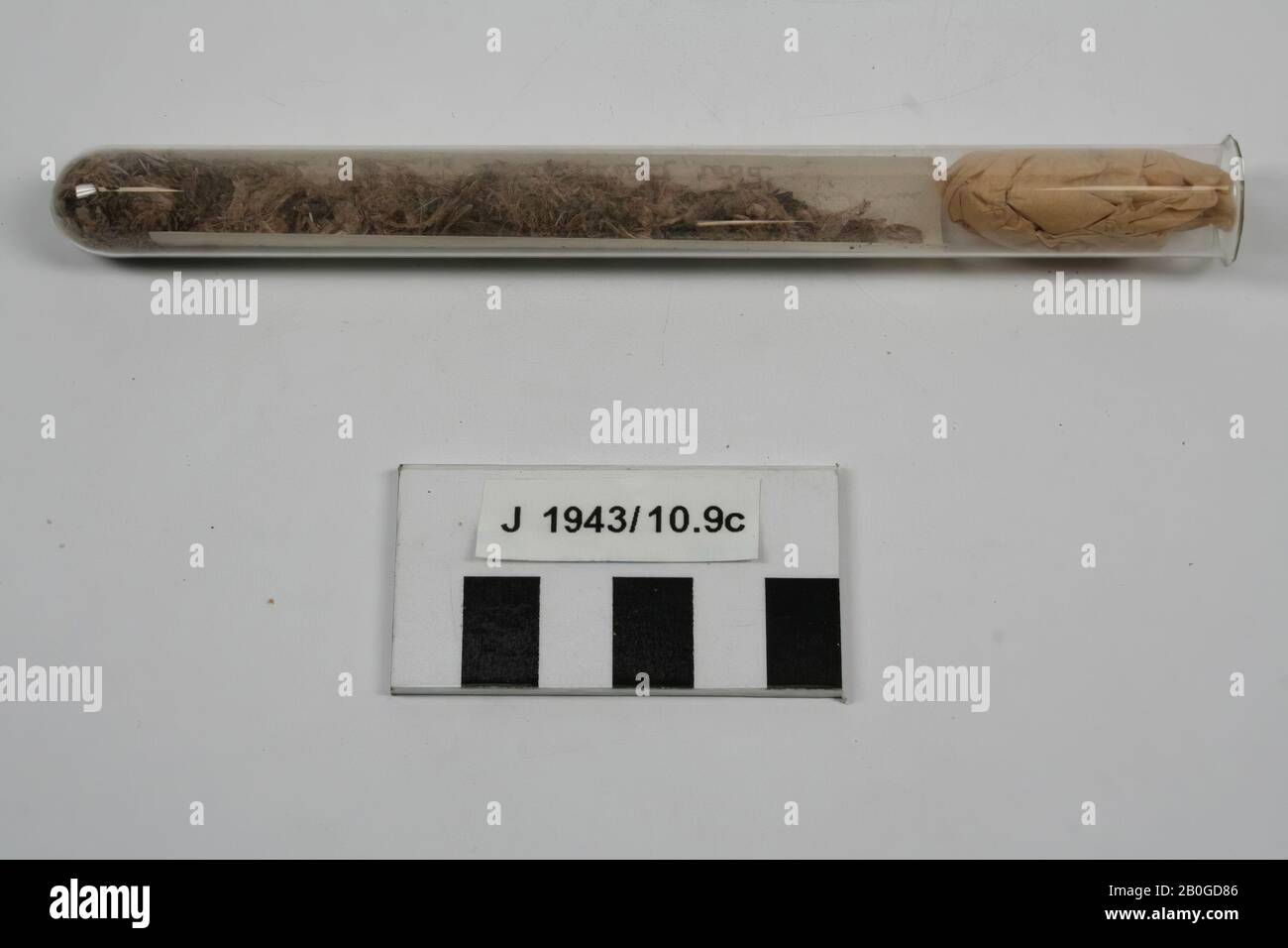 Glass test tube filled with fragments of textiles, a wad of paper and a ...