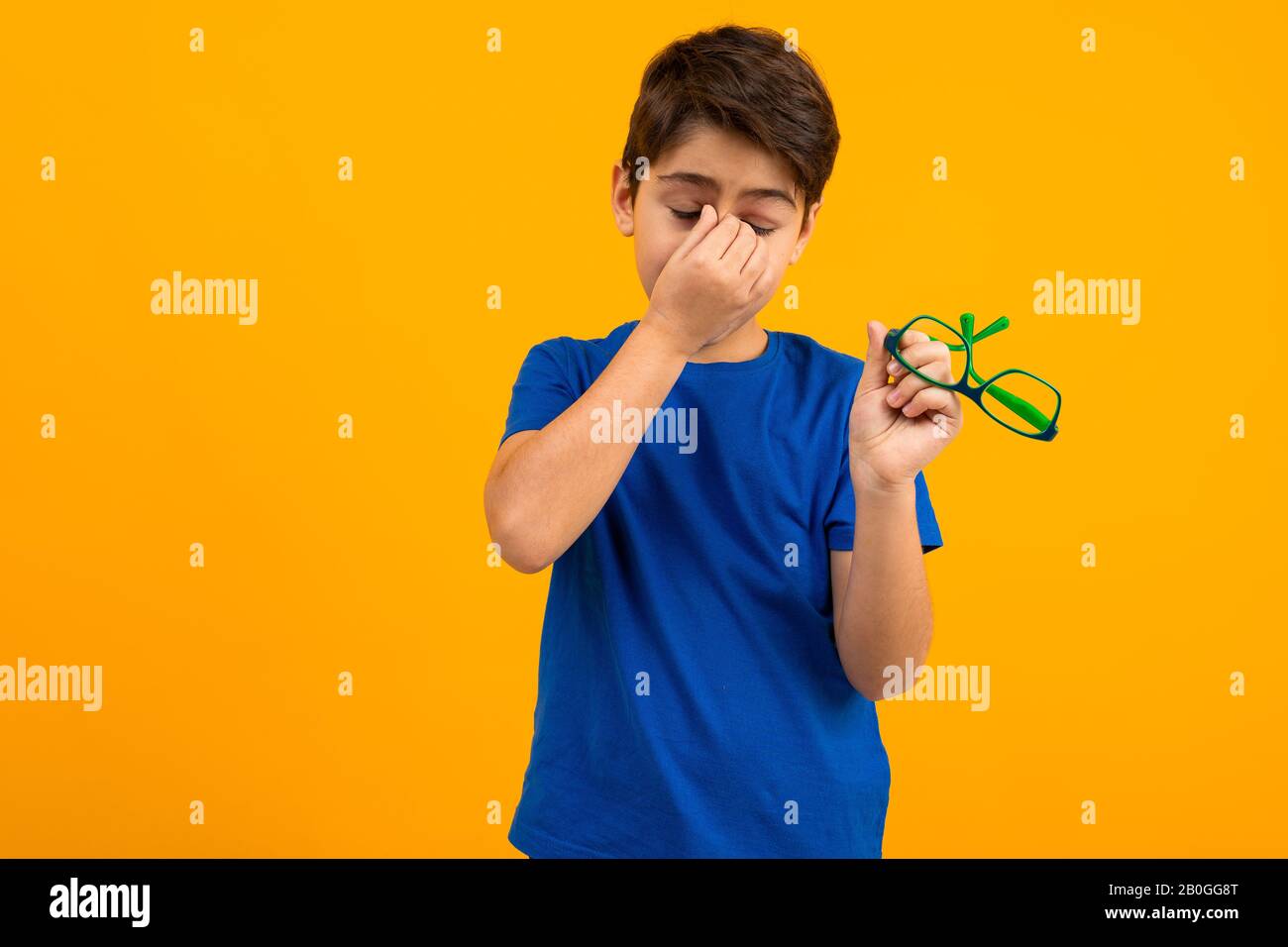 a boy in a blue T-shirt holds glasses in his hand and rubs his eyes on ...