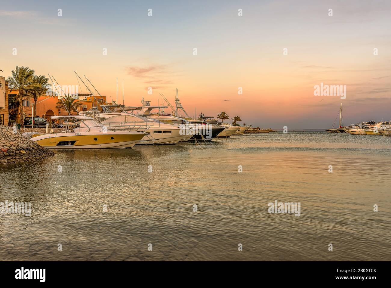 Motor yachts at anchor in the sunset with orange sky and illuminated ...