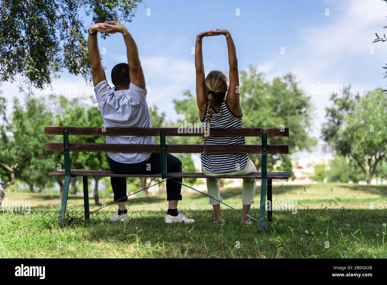 Young couple sitting on a wooden bench under a tree with their arms ...