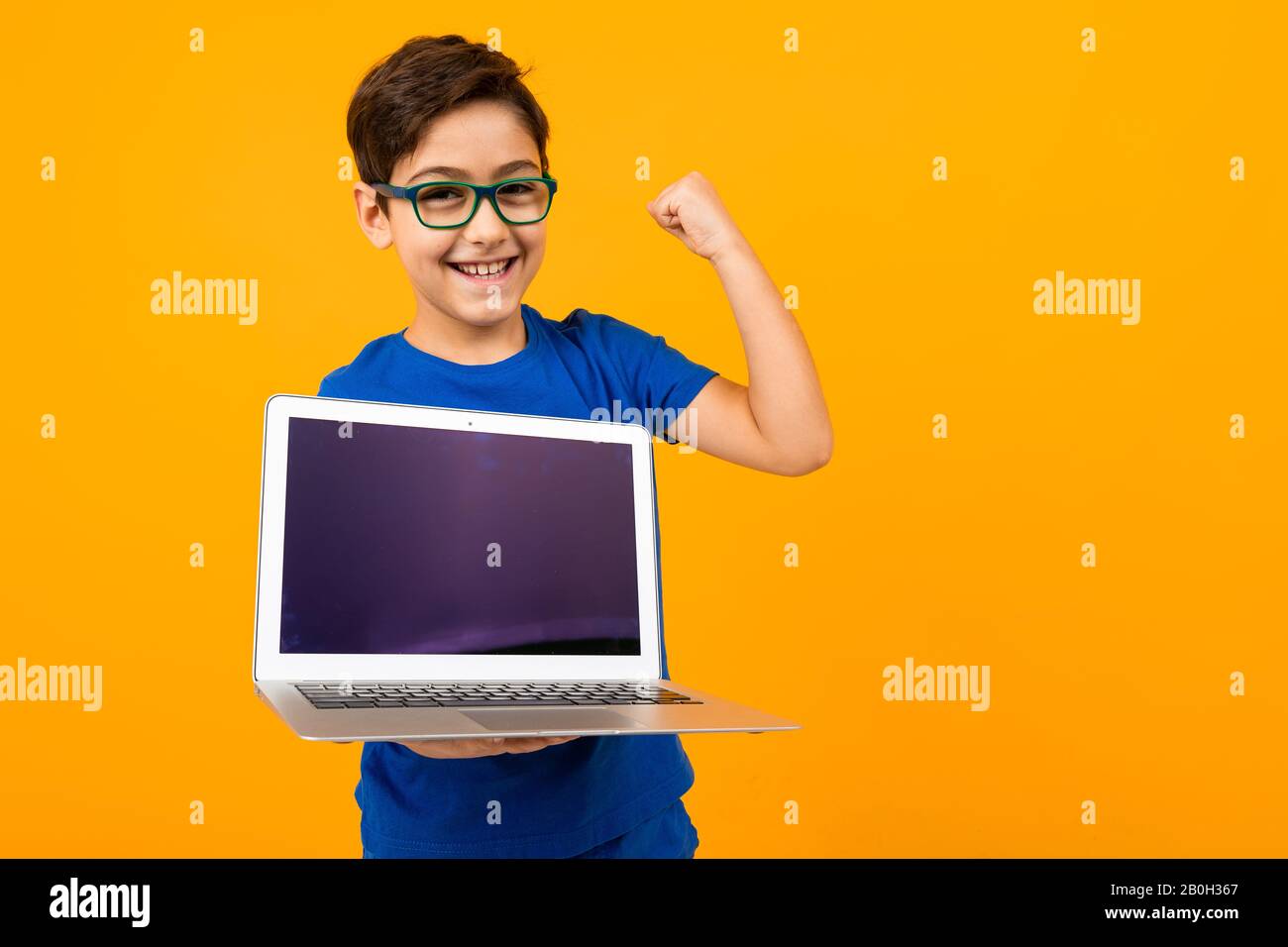 joyful caucasian boy shows laptop screen with mockup on yellow studio ...