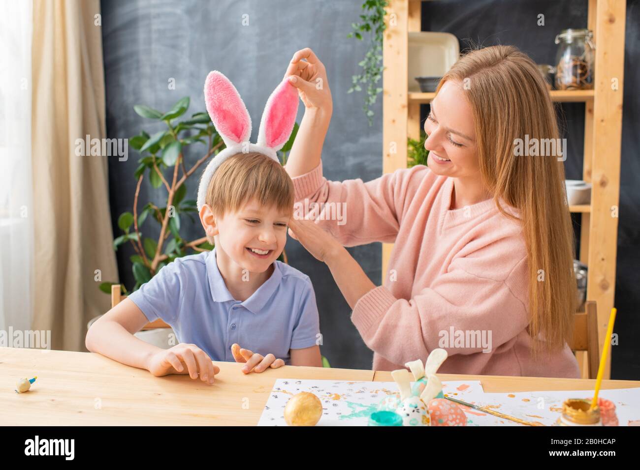 Happy young mother adjusting rabbit ears headband on son head while ...