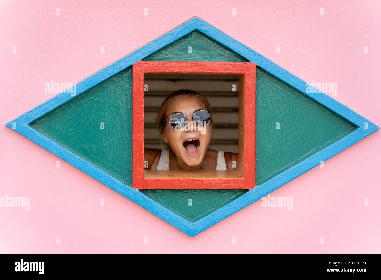 Blonde girl with sunglasses sticking her head out of a small window ...