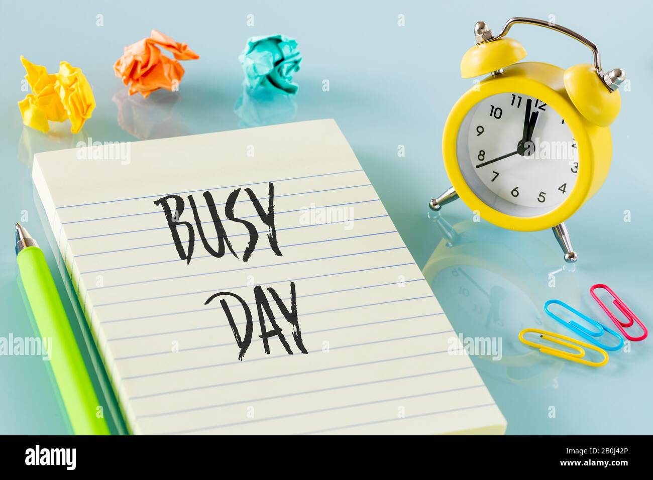 yellow alarm clock next to the notebook with the words "busy day ...