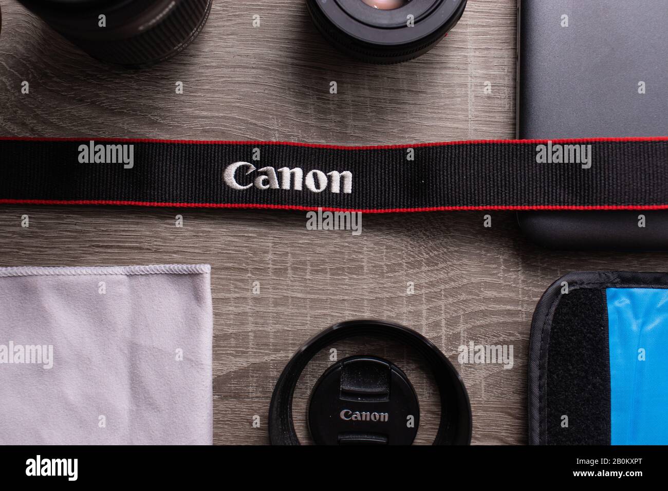 Photography flat lay on a grey wood table. Canon black strap with red ...