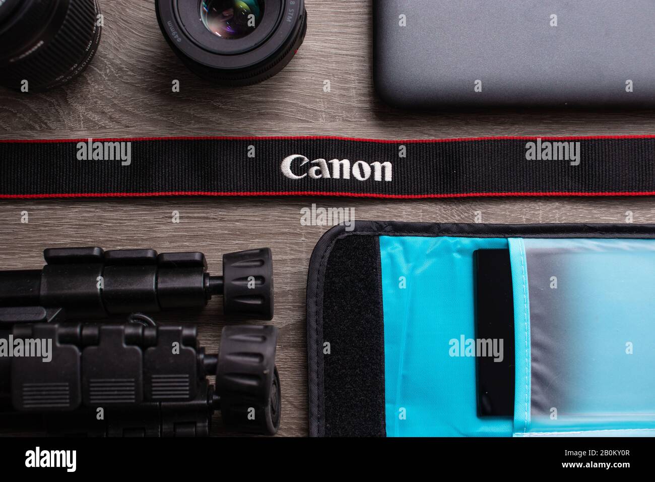 Photography flat lay on a grey wood table. Canon black strap with red ...