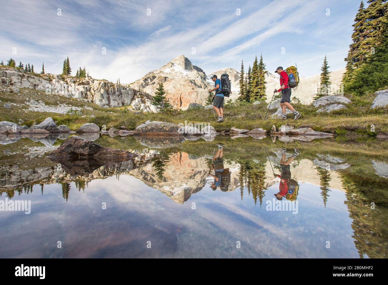 Side view and reflection of backpackers hiking beside alpine lake Stock ...