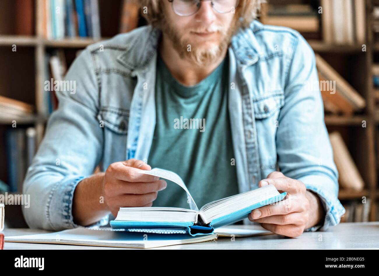 Closeup young man home library desk open read book turn page education ...
