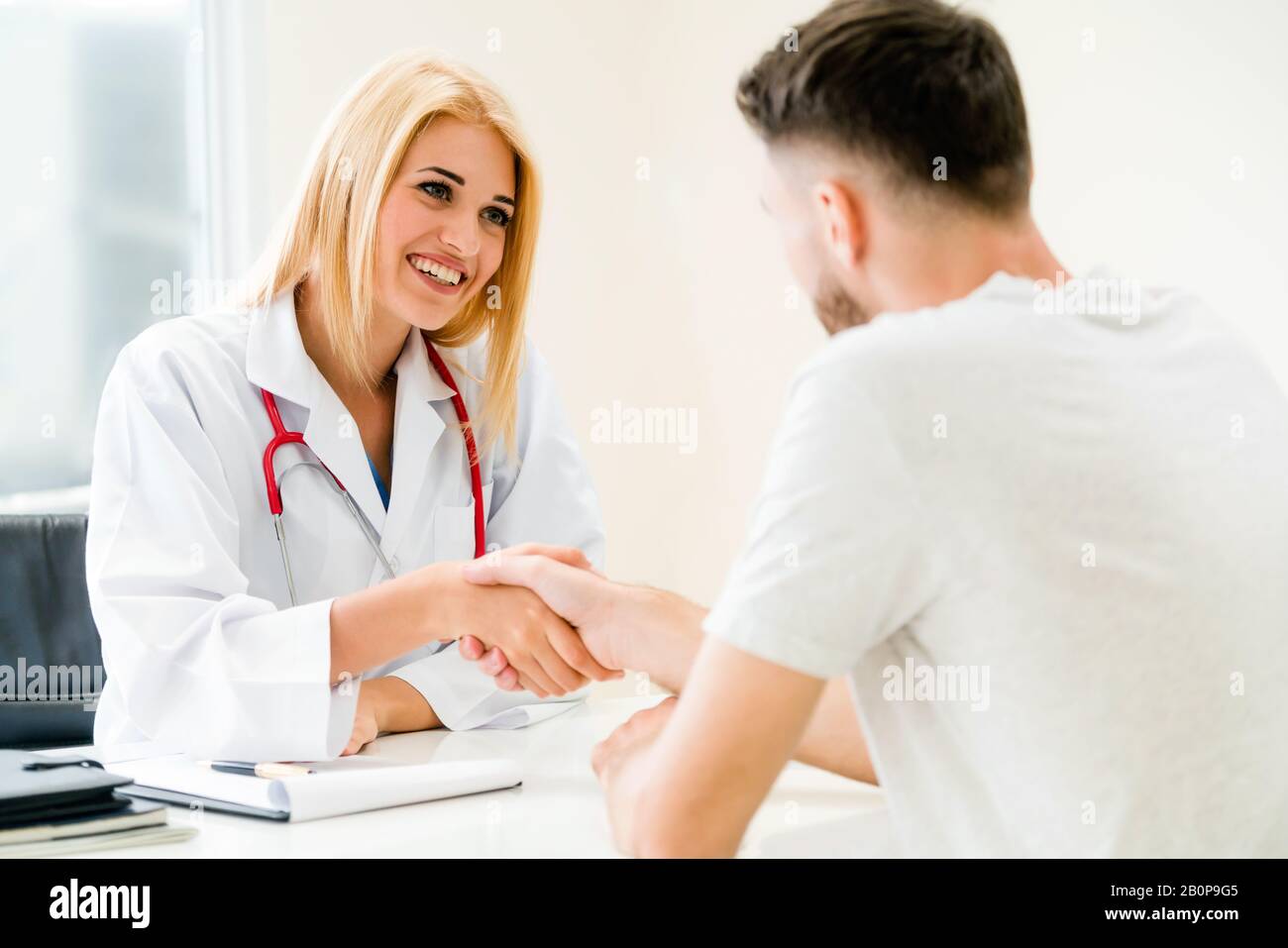 Woman doctor doing handshake with male patient in hospital office room ...