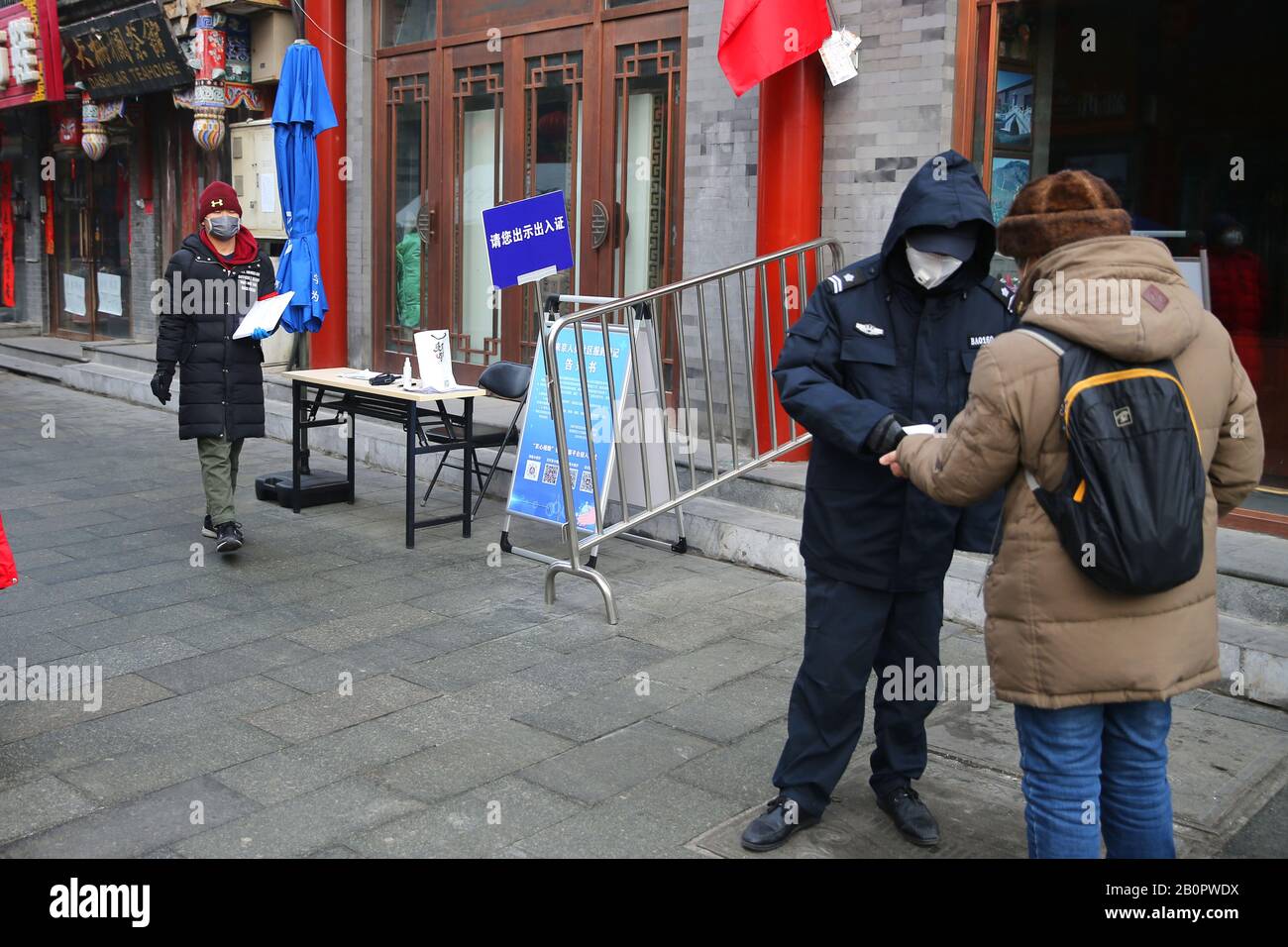 A masked Chinese security guard checks the body temperature of a ...