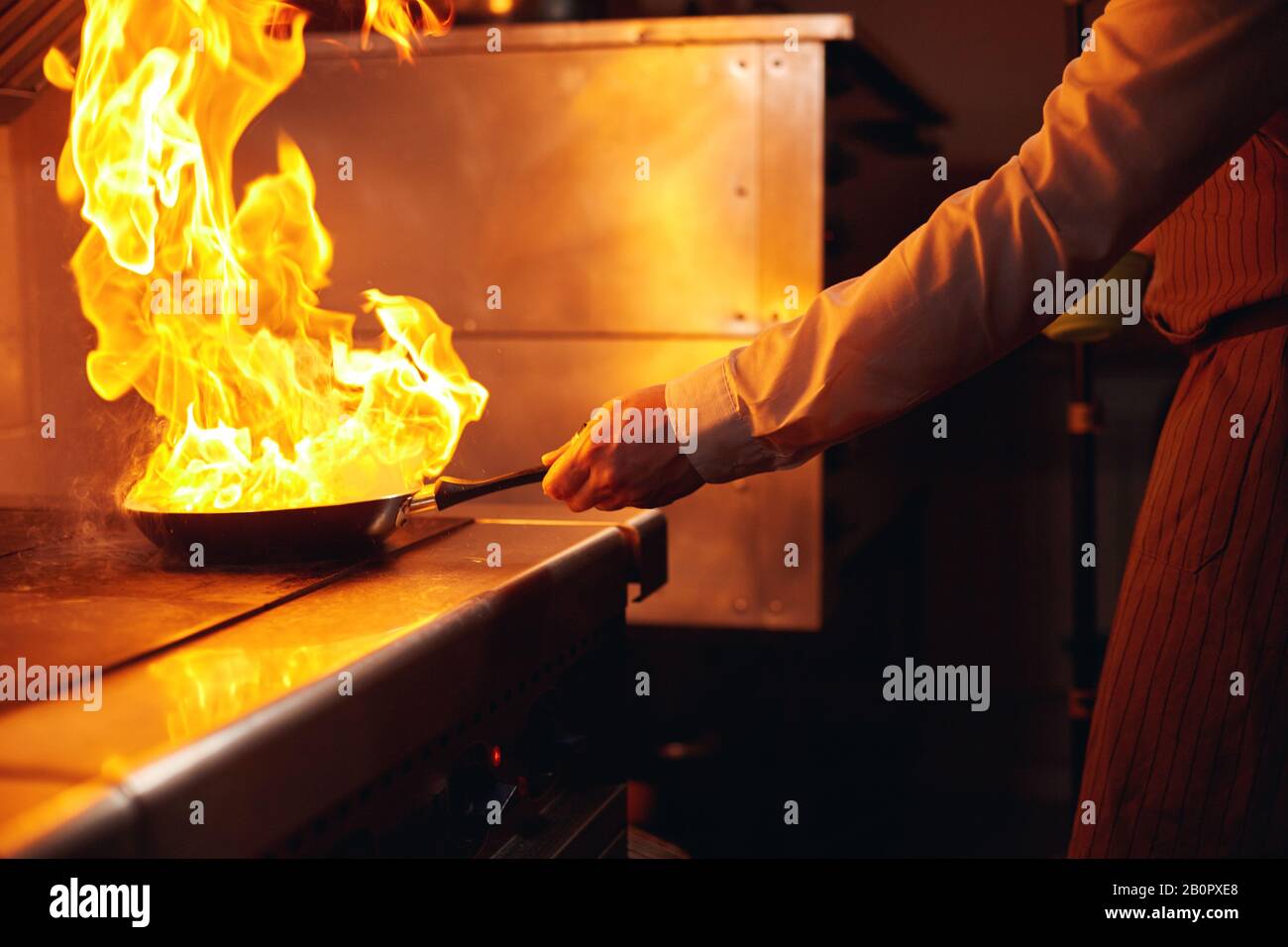 Flambe. Fire in frying pan. Professional chef in a commercial kitchen ...