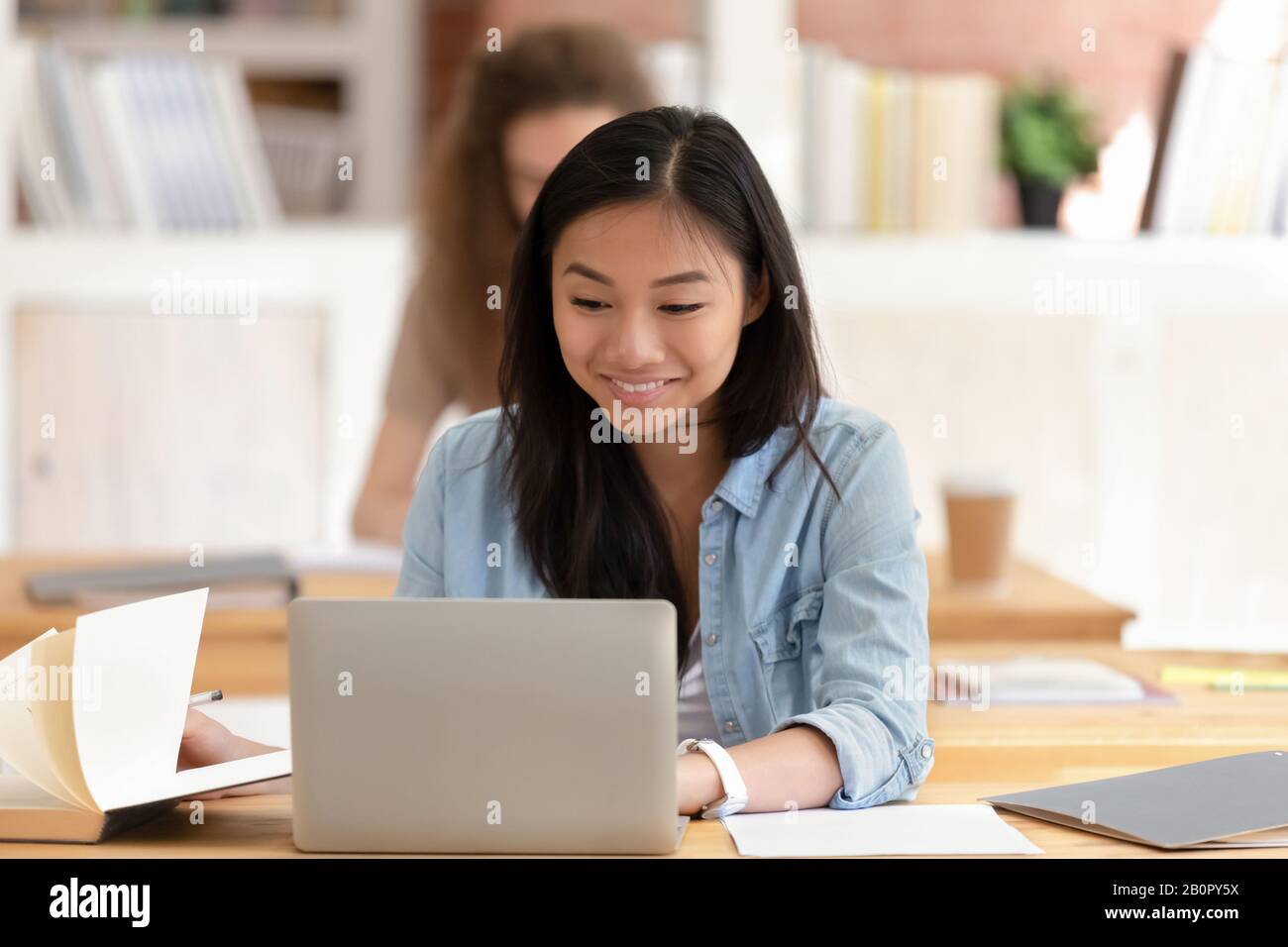 Smiling Asian female student studying, using laptop in college ...