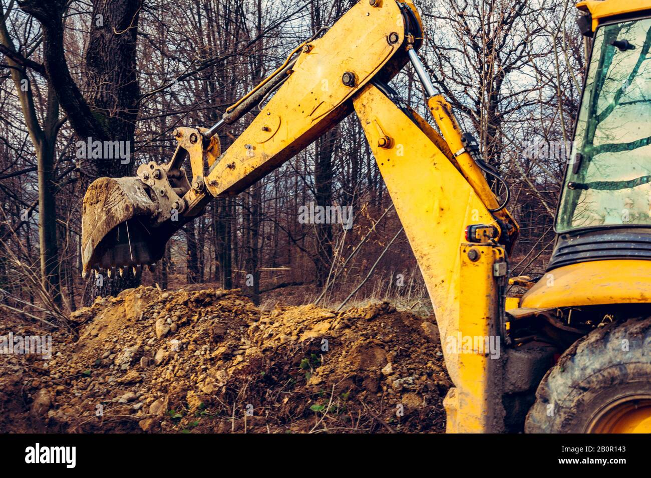 Worker and yellow old excavator in the forest dig a pit for water ...