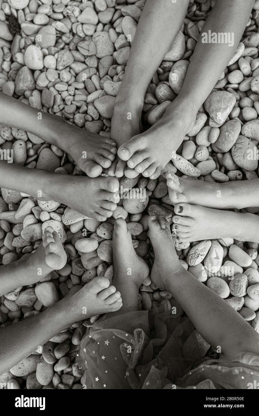 Monochrome image of legs of five kids in a circle over small pebbles ...