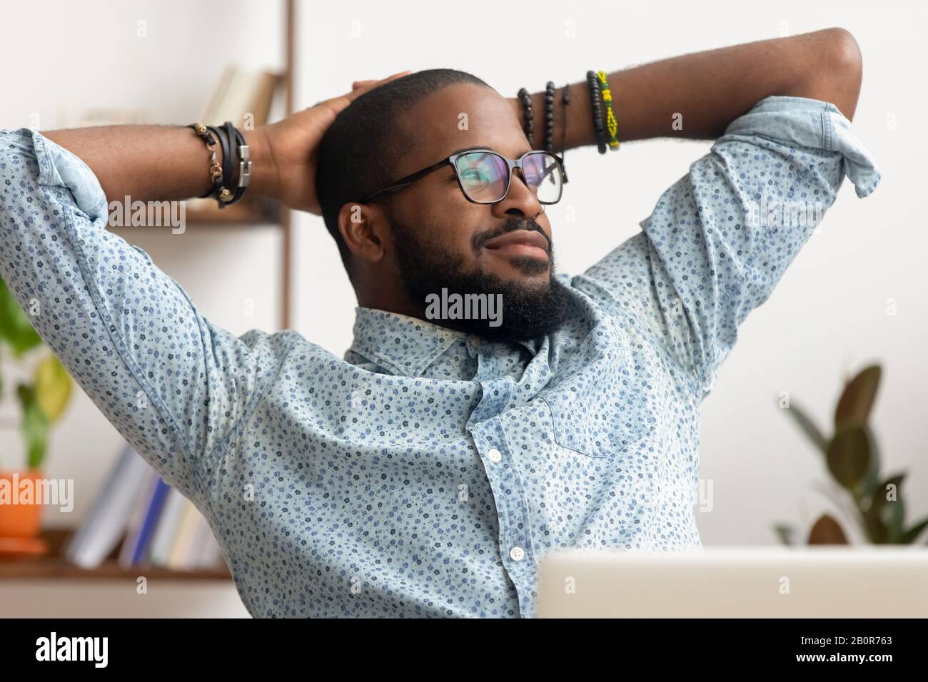 Dreamy African American businessman with hands behind head relaxing ...