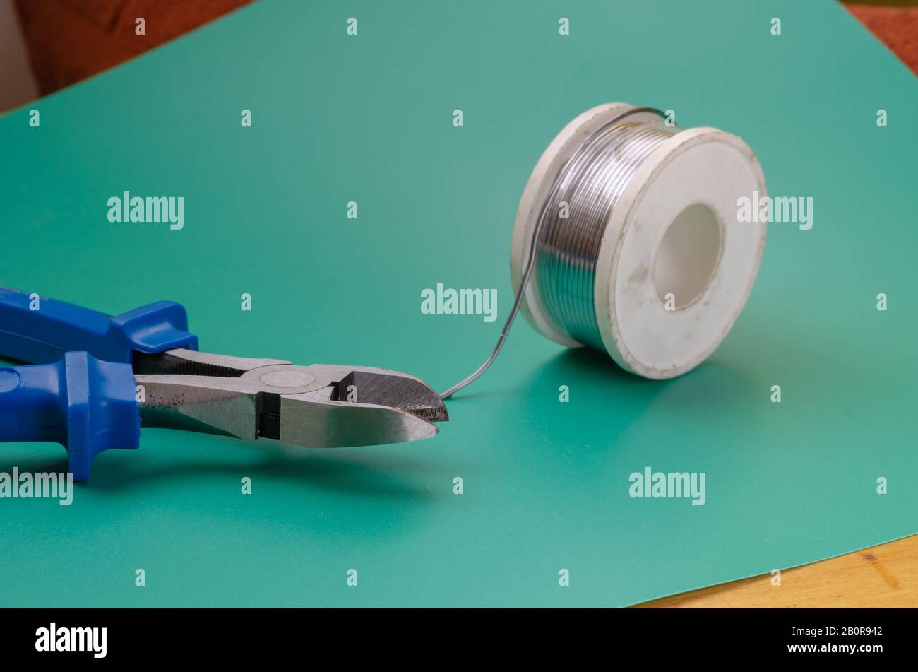 Side view of wire cutters with blue handles and a dirty coil of solder ...