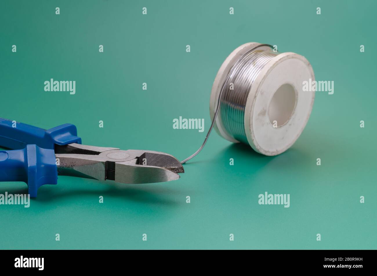 Side view of wire cutters with blue handles and a dirty coil of solder ...