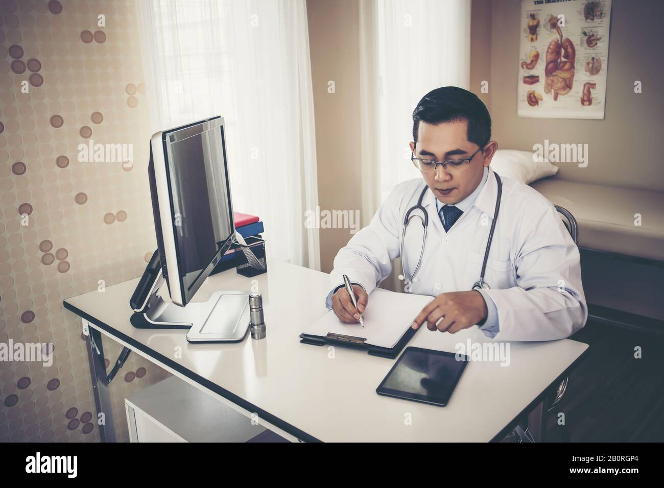 Doctor is working with documents in front of his computer in his ...