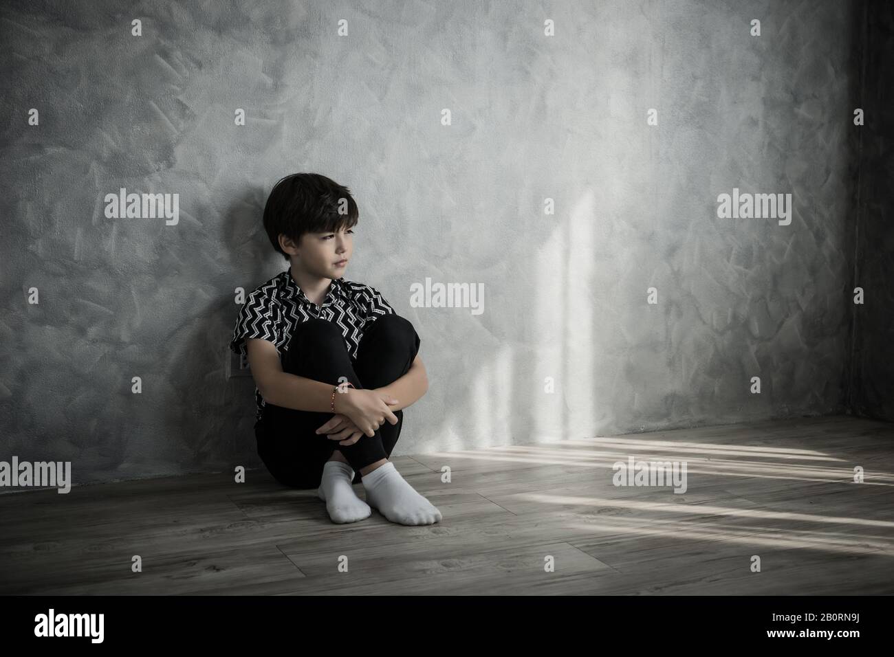 Sad boy sitting thinking sitting on the floor of the room against the ...