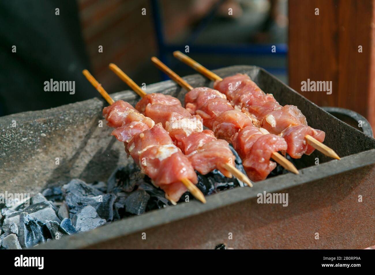 A fresh pork mini barbeque on the wooden sticks is cooking on the hot ...