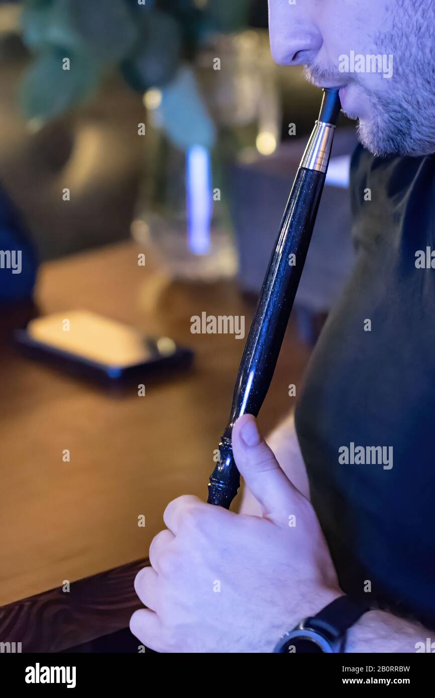 Close-up of a man smoking a traditional hookah pipe, man exudes smoke ...