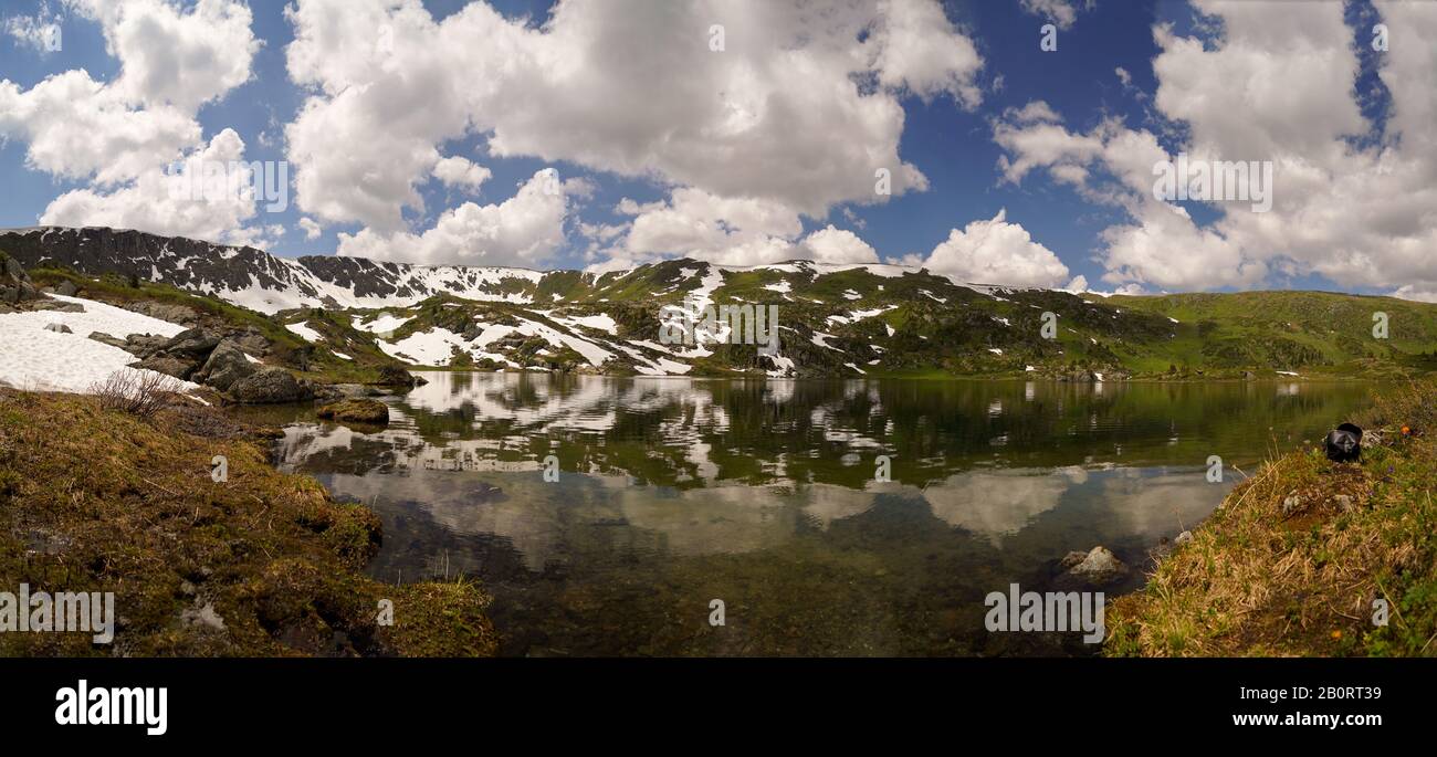 Lake in mountain dale with wild herbs and showbanks on the shores and ...
