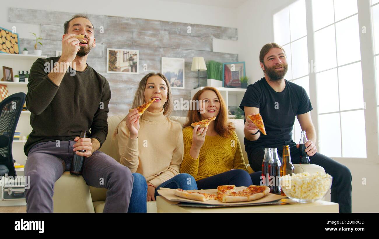 Group of friends sitting on couch in living room and browsing on their ...