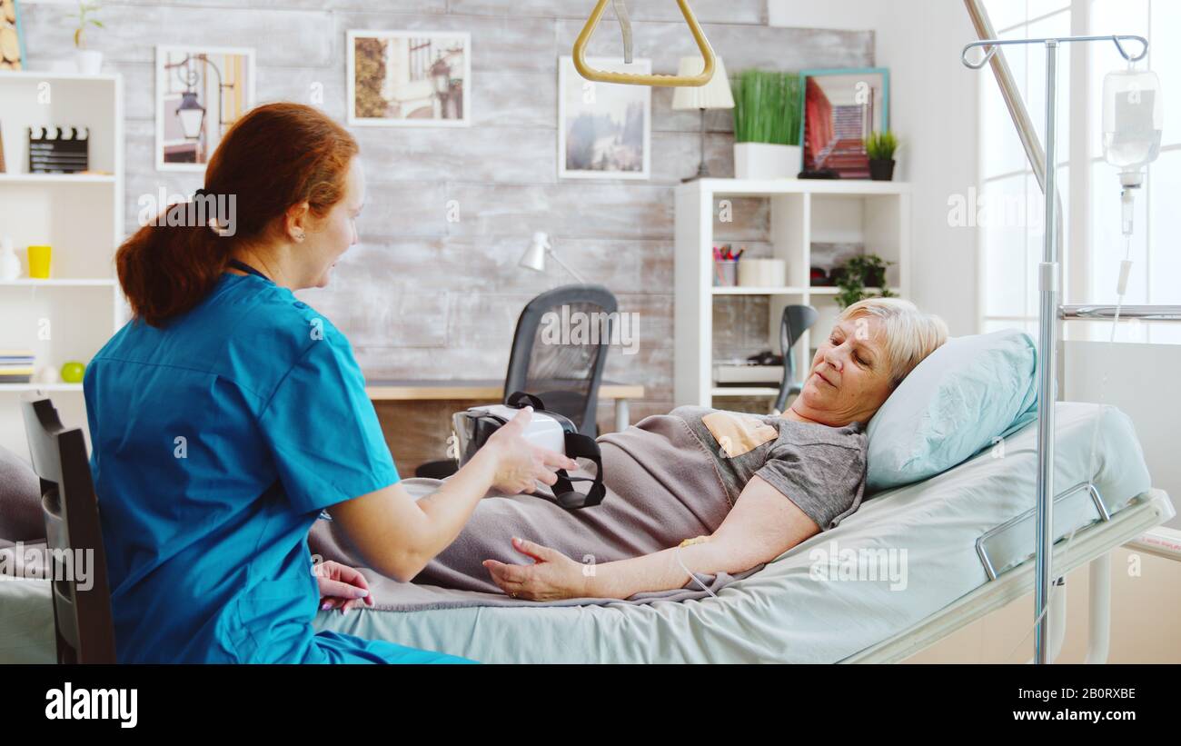 Female nurse in retirement home giving an old disabled lady a VR ...