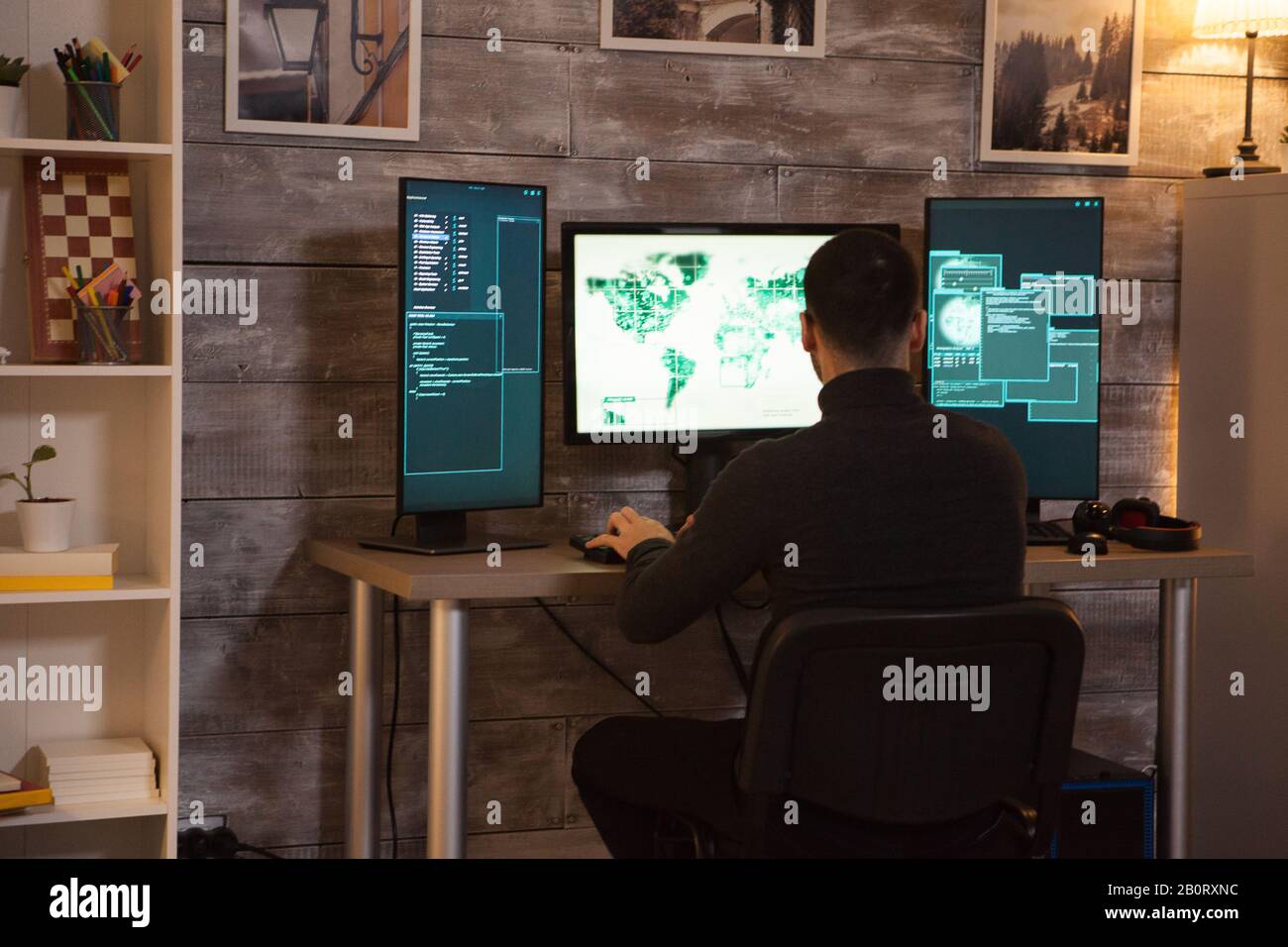 Back view of young hacker sitting on desk writing a malware for ...