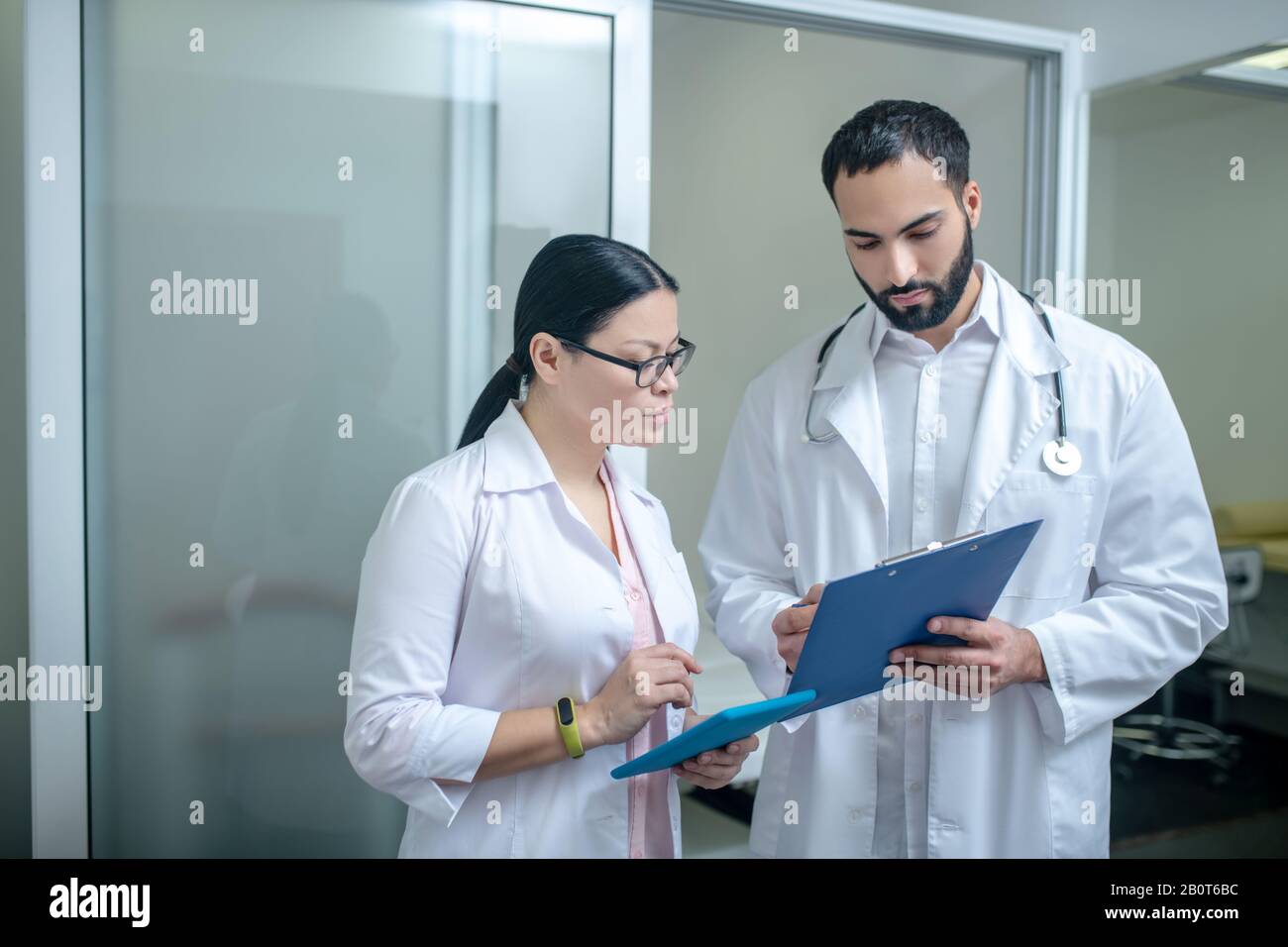 Dark-haired male and female doctors standing in the room together ...