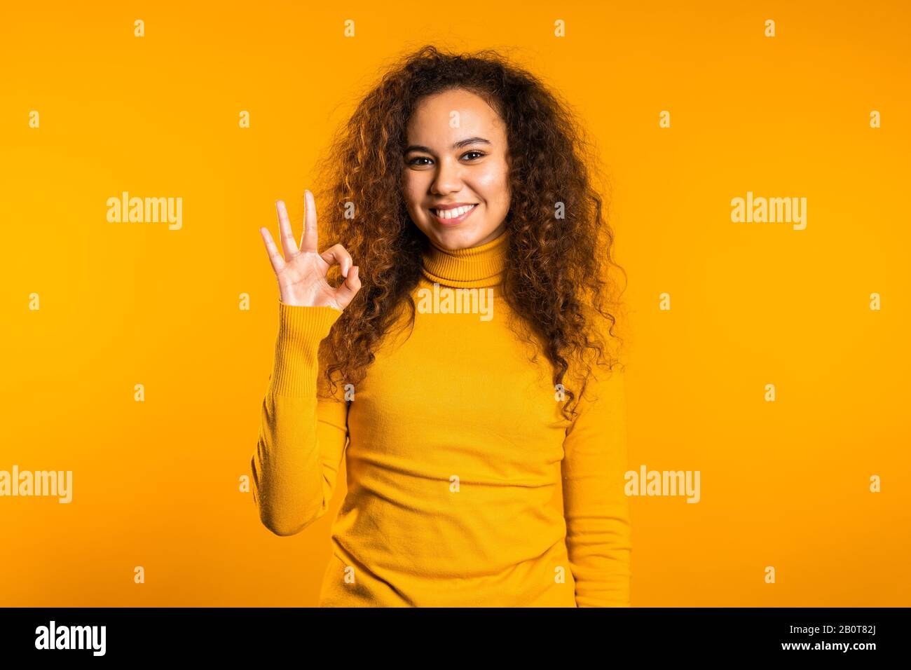 Positive girl making OK sign over yellow background and smiles to ...