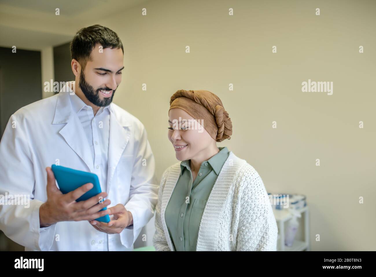 Bearded young doctor showing something on the tablet to his patient ...