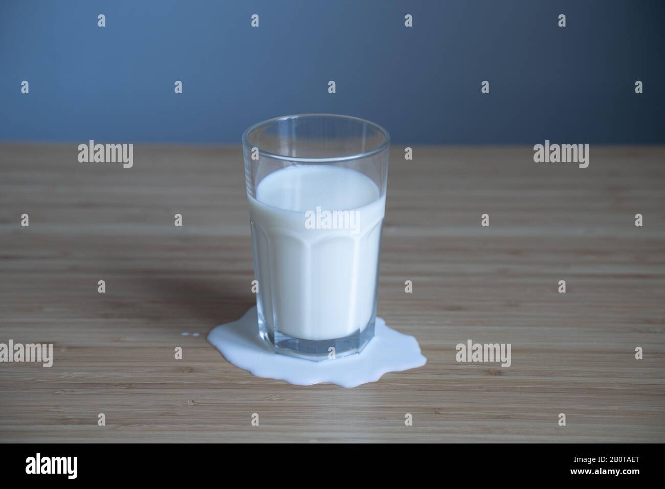 front view closeup of glass in a puddle of spilled milk on light ...