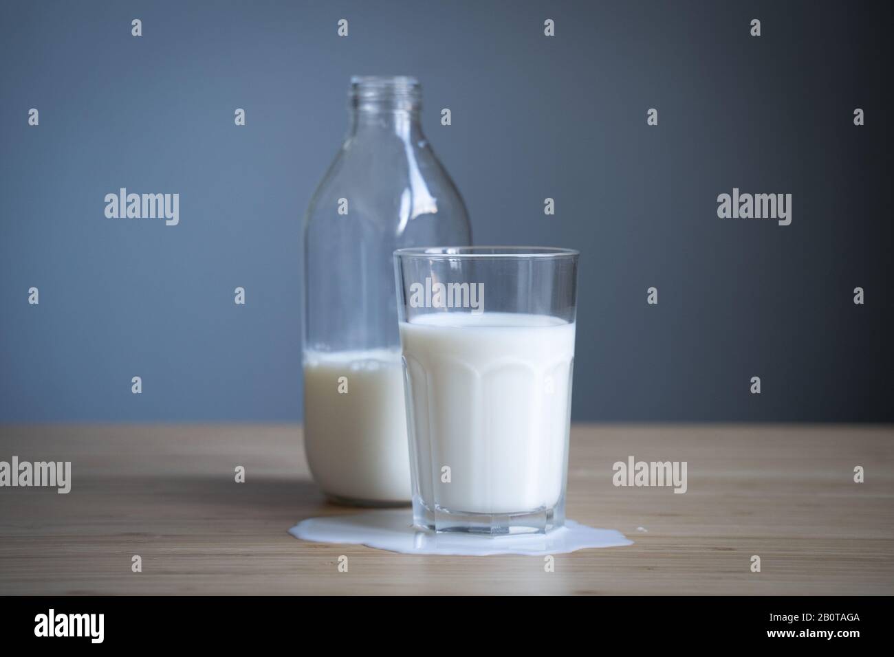 front view closeup of glass bottle in a puddle of spilled milk on light ...