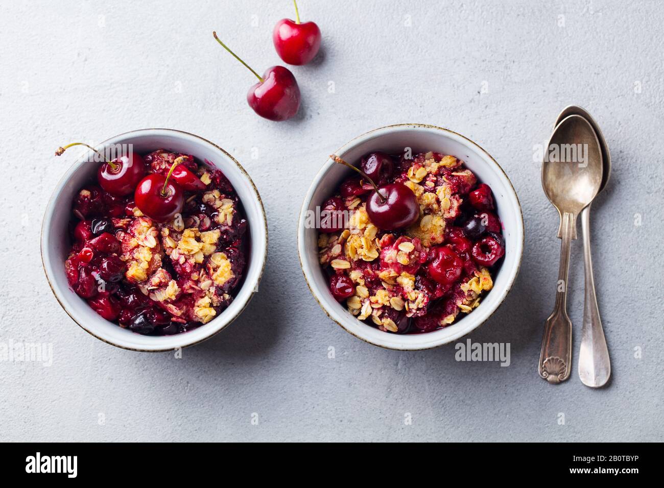 Cherry, red berry crumble in bowl. Grey stone background. Top view ...