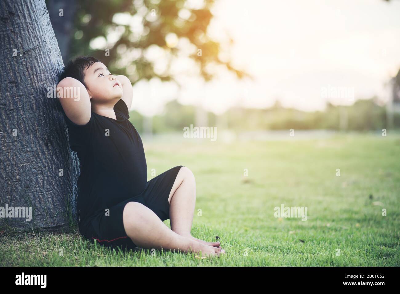 Little boy sitting under the tree thinking something Stock Photo - Alamy