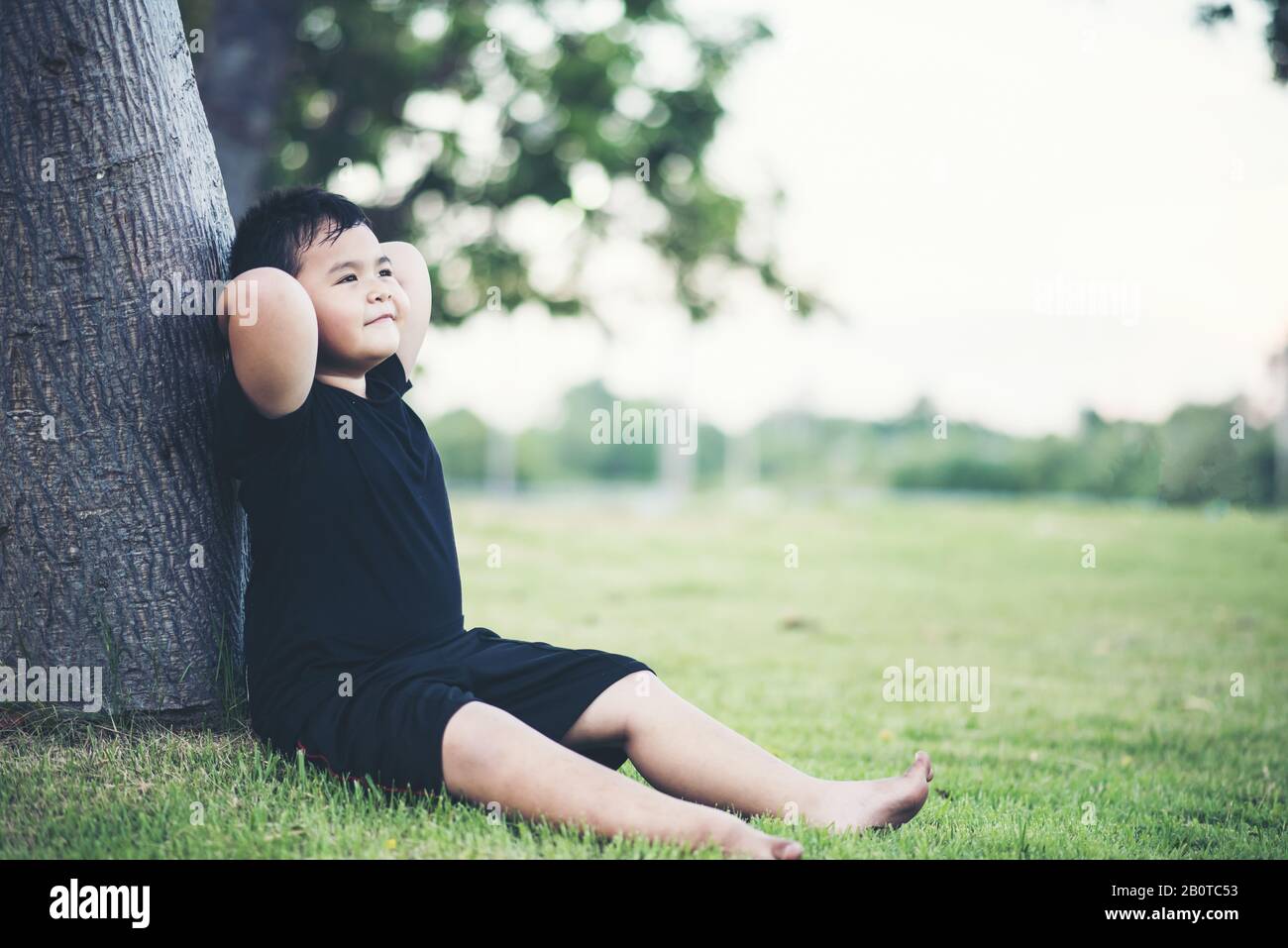 Little boy sitting under the tree thinking something Stock Photo - Alamy