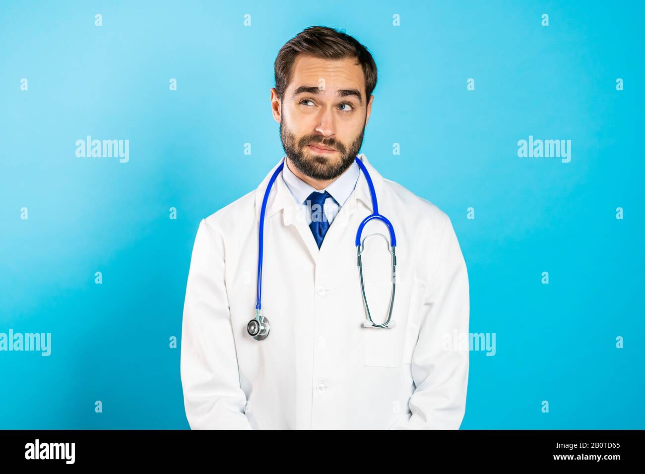 Thinking doctor man looking up and around on blue background. Worried ...