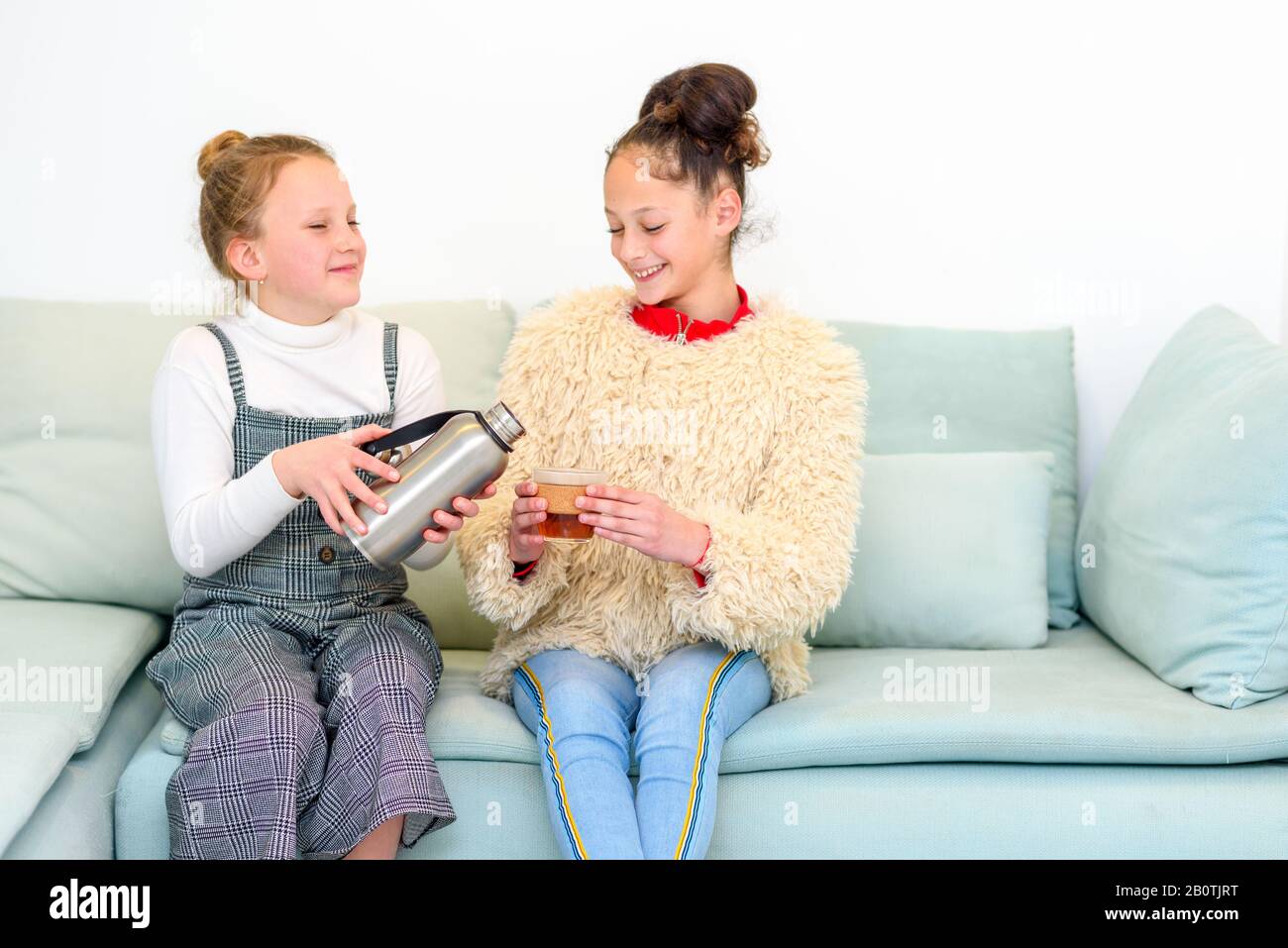 Teenage girls talking, laughing and pouring tea to reusable glass cup ...