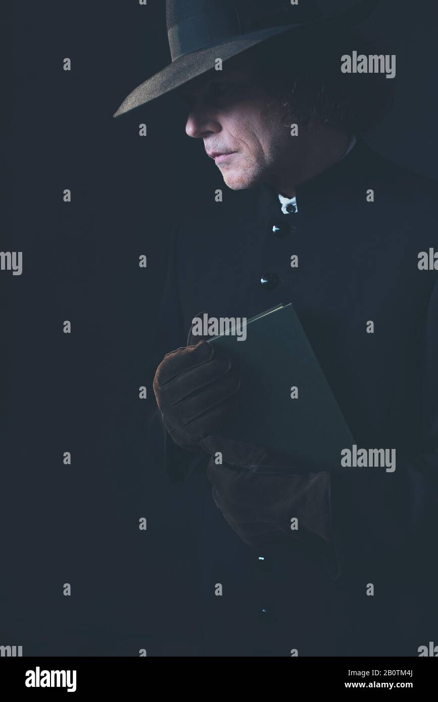 Mysterious victorian priest in hat holding book Stock Photo - Alamy