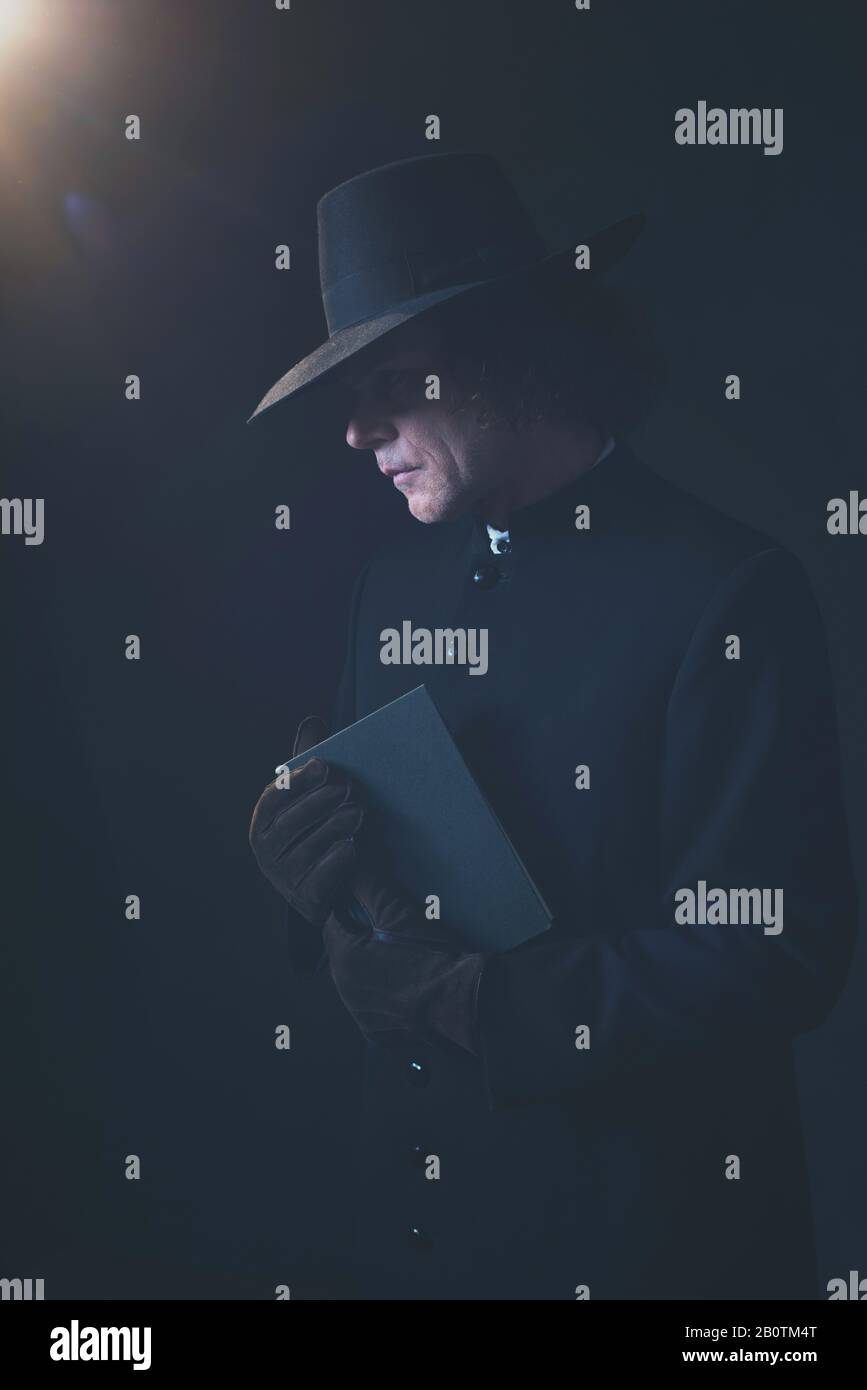 Mysterious victorian priest in hat holding book Stock Photo - Alamy