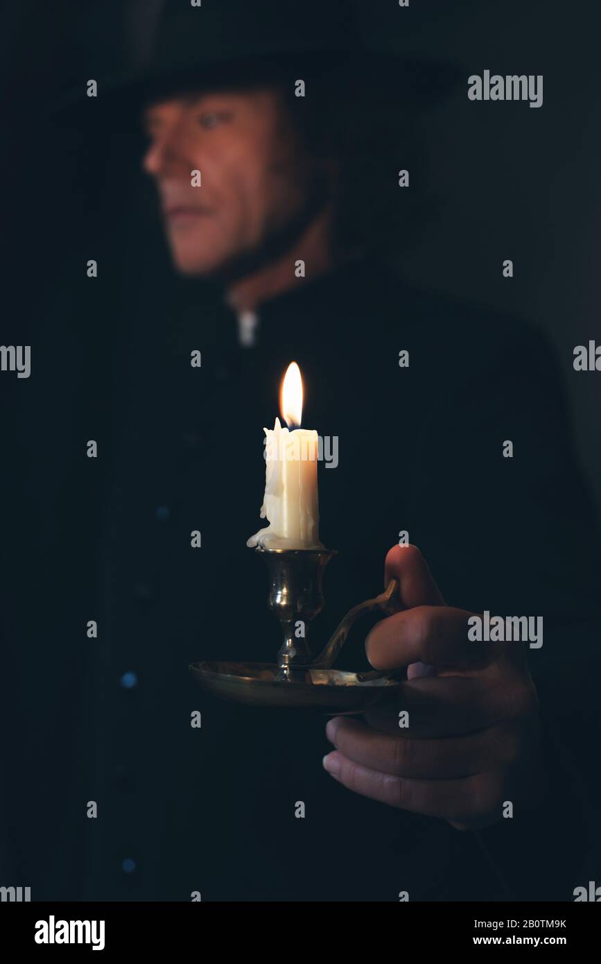 Mysterious victorian priest in black coat and hat holding candlestick ...