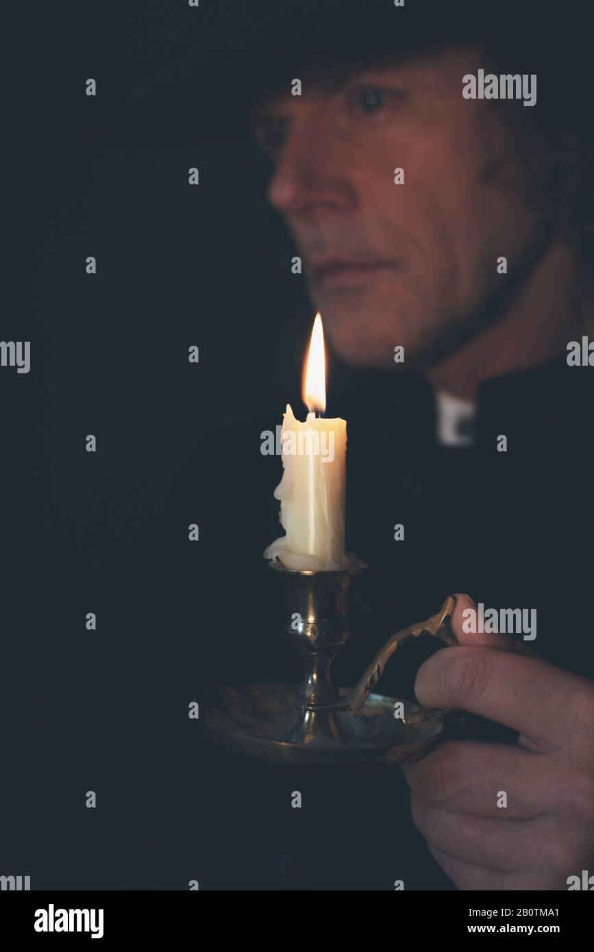 Mysterious victorian priest in black coat and hat holding candlestick ...