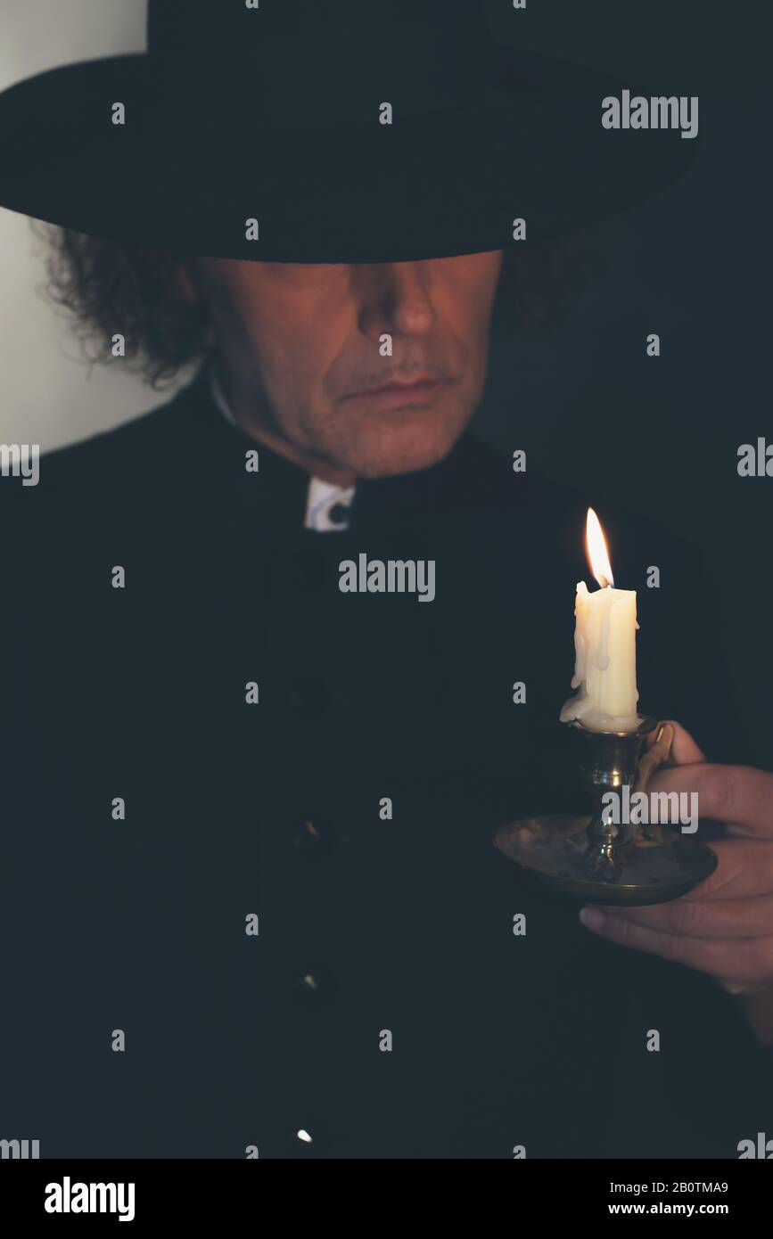 Mysterious victorian priest in black coat and hat holding candlestick ...