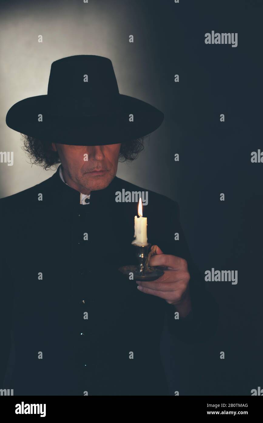 Mysterious victorian priest in black coat and hat holding candlestick ...