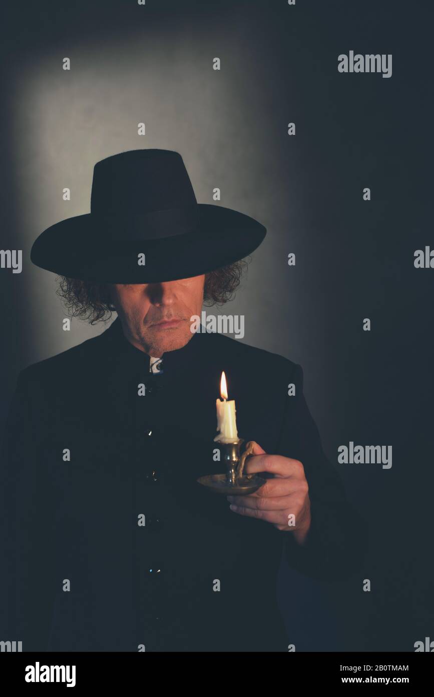 Mysterious victorian priest in black coat and hat holding candlestick ...